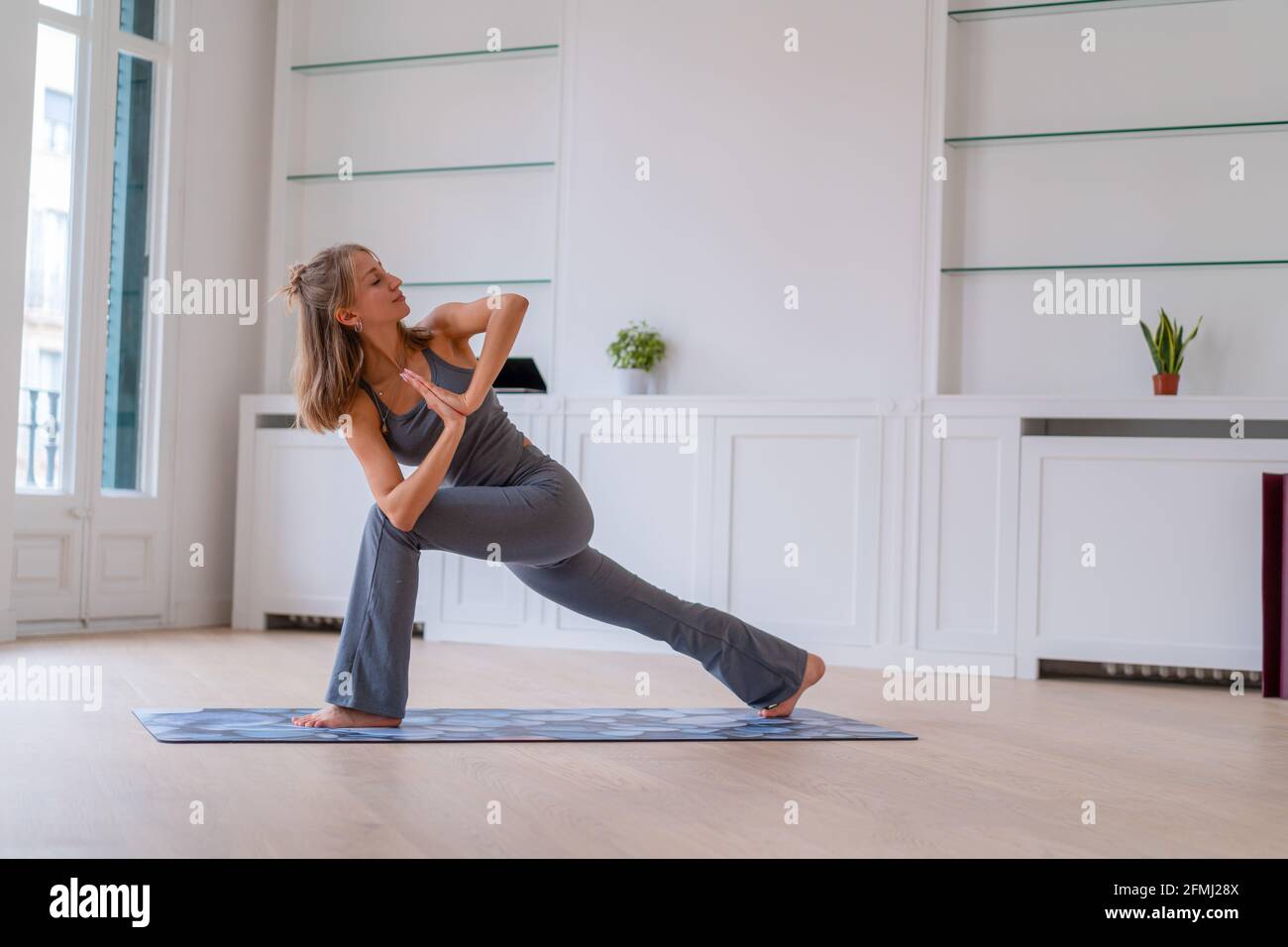 Side view of fit flexible female standing on mat in Revolved Warrior ...