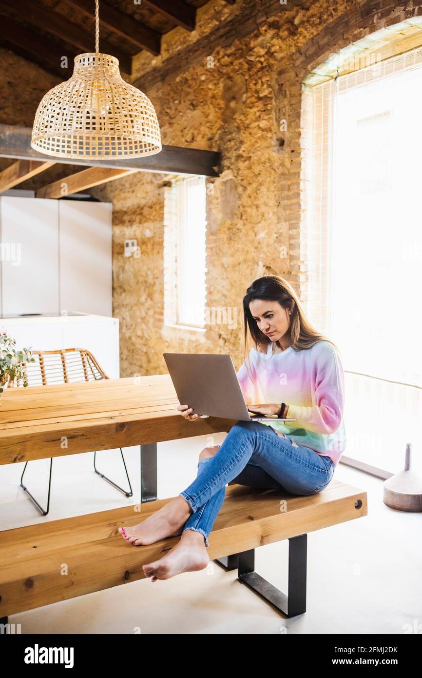Barefoot female distance employee typing on netbook while sitting with ...