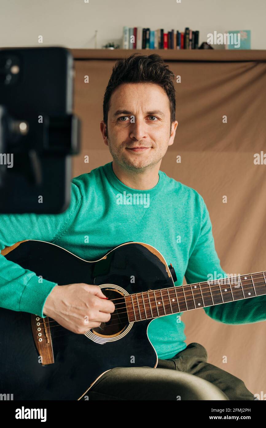 Crop cheerful adult male vlogger with guitar and plectrum recording ...