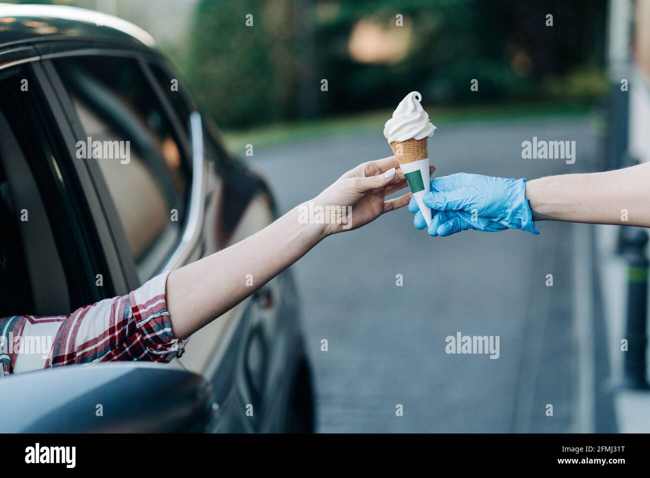 Crop unrecognizable female sitting in car and taking ice cream in drive ...