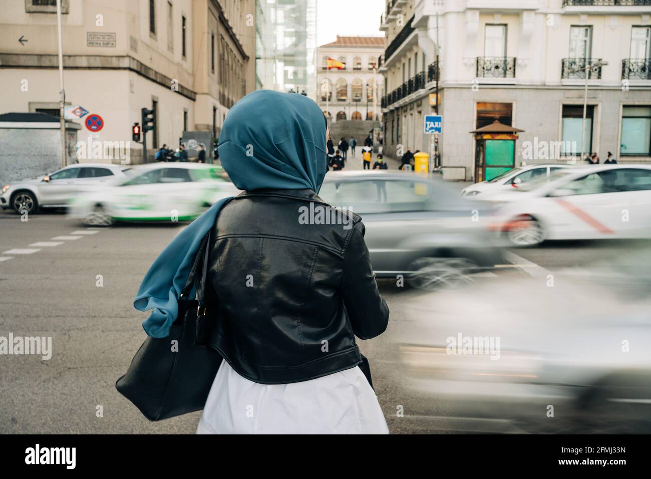 Back view of anonymous Muslim female in hijab standing near road with ...