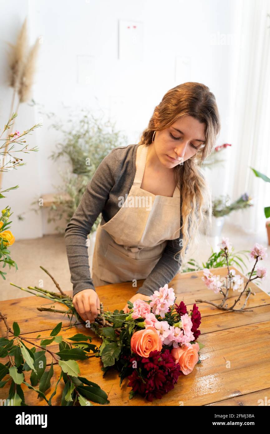 Concentrated young female florist with long wavy hair in casual clothes ...