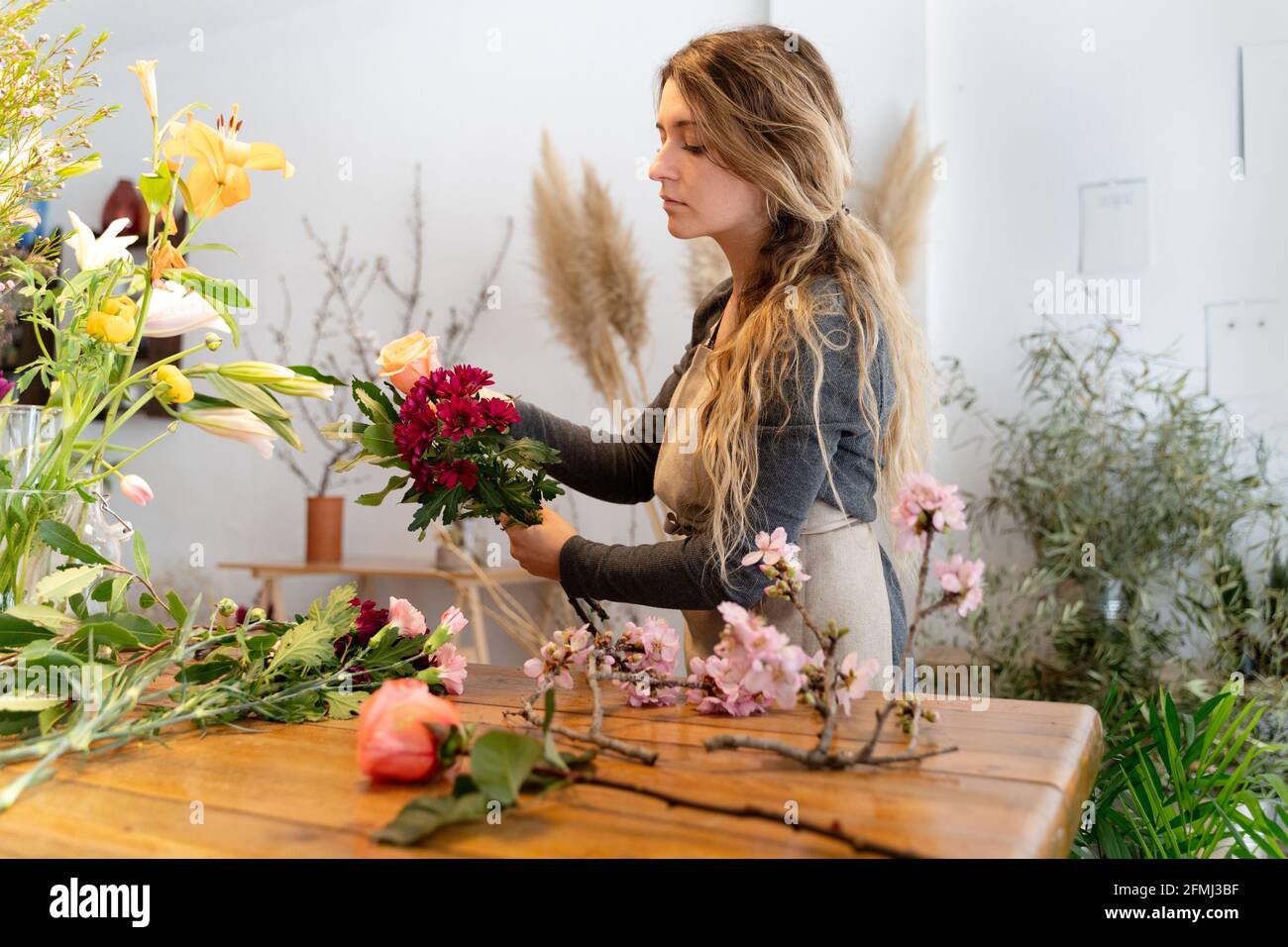 Concentrated young female florist with long wavy hair in casual clothes ...