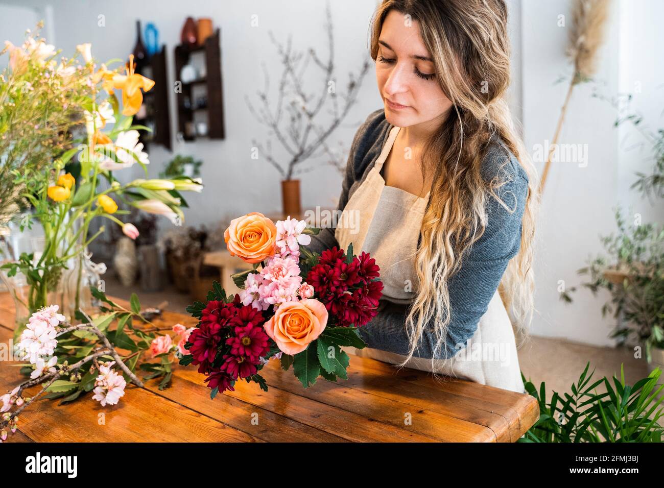 Concentrated young female florist with long wavy hair in casual clothes ...