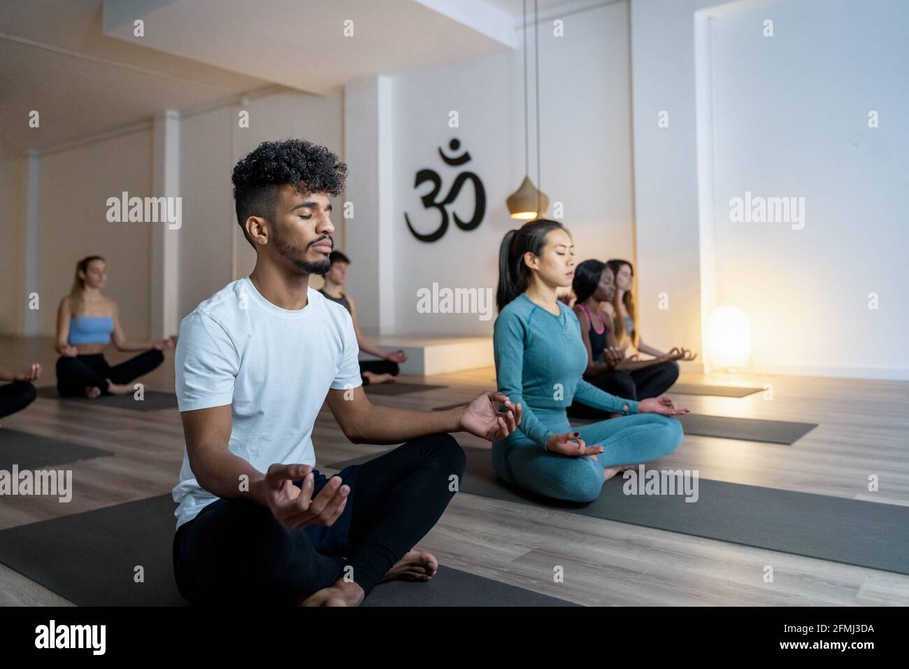 African American man with group of diverse people sitting in Lotus pose ...