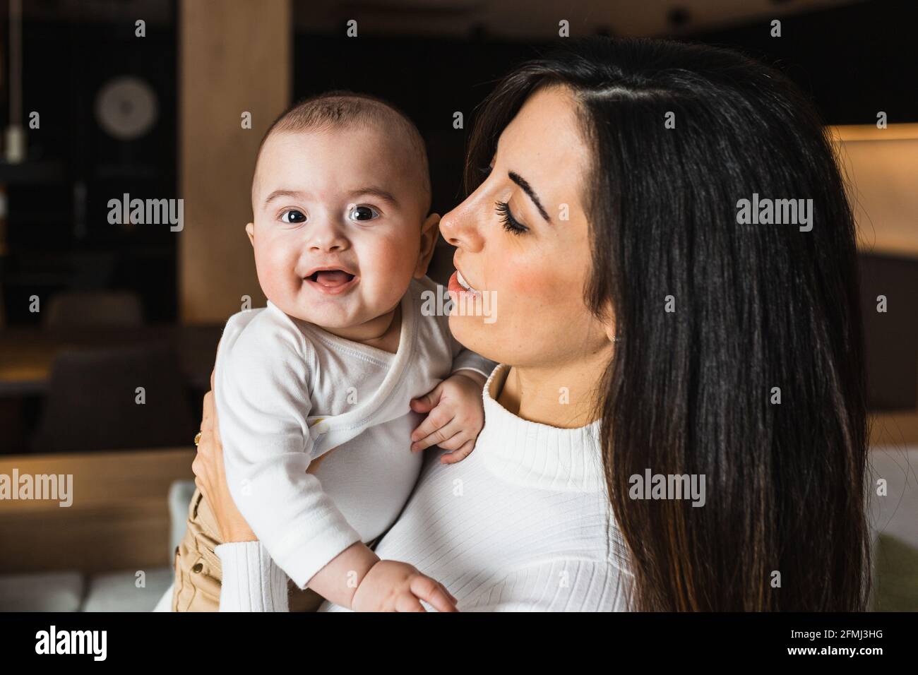 Side view of delighted mother holding adorable smiling baby while ...