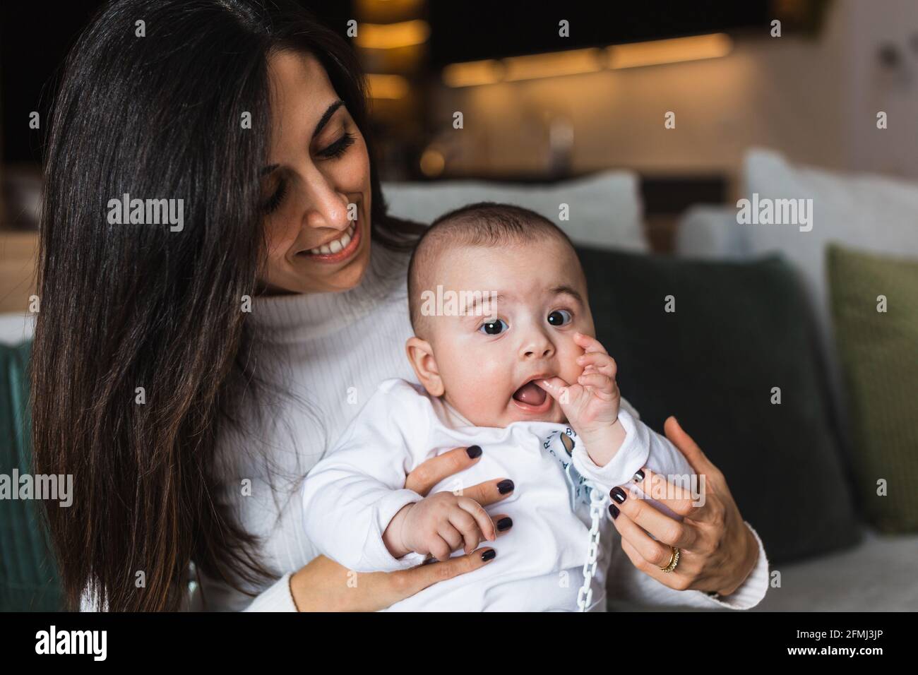 Delighted mother holding adorable smiling baby while having fun ...