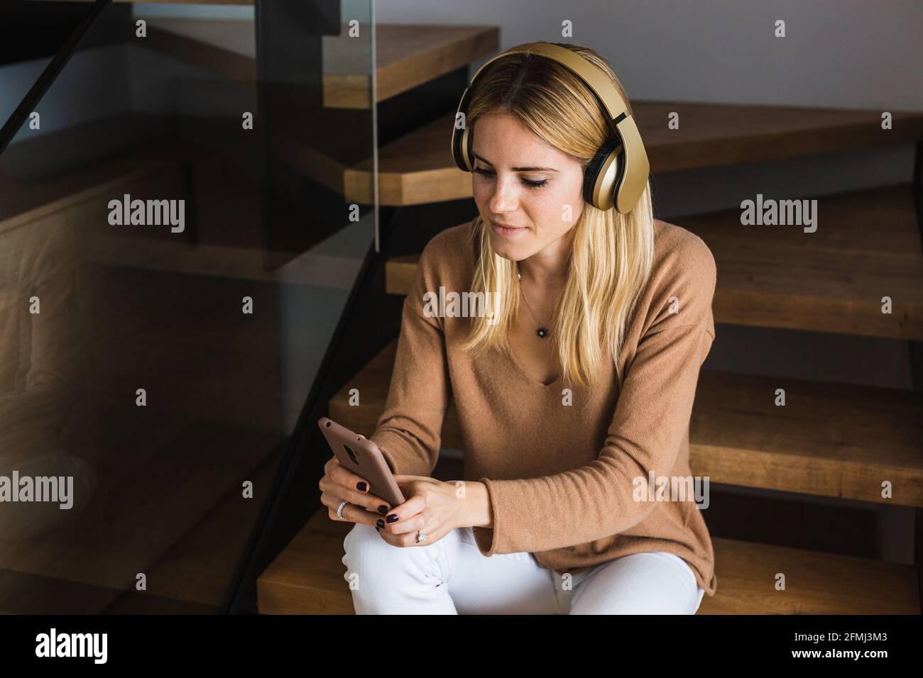 Cheerful female in headphones enjoying songs while sitting on stairs at ...