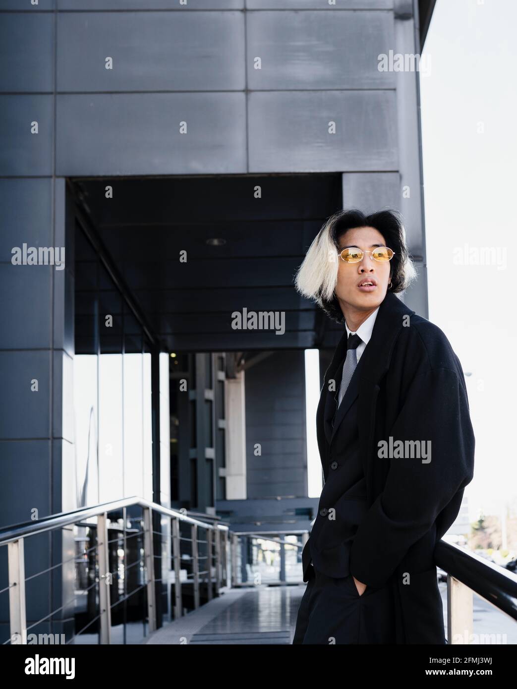 Young Asian male executive in suit and sunglasses with hands in pockets ...