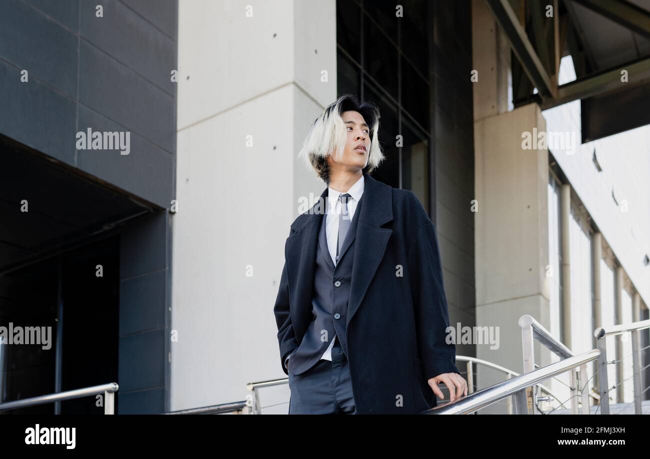 Young Asian male executive in suit with hands in pockets looking away ...