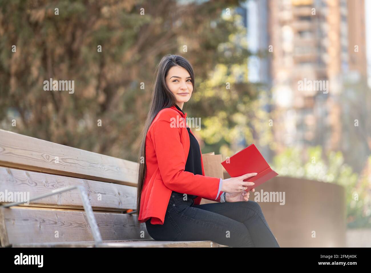 Smiling female customer sitting on bench with paper bags and reading ...