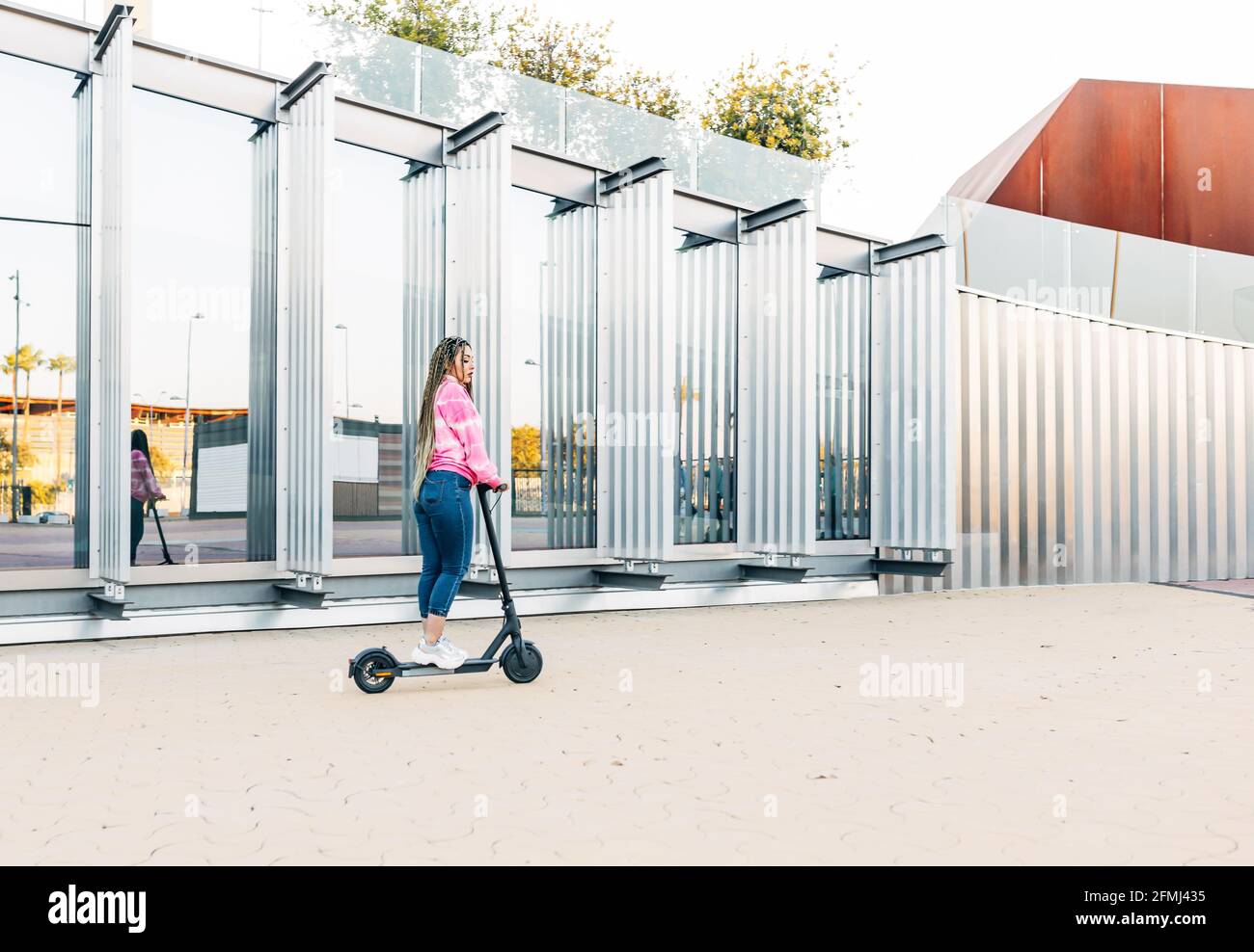 Side view of millennial female in trendy wear riding electric scooter ...