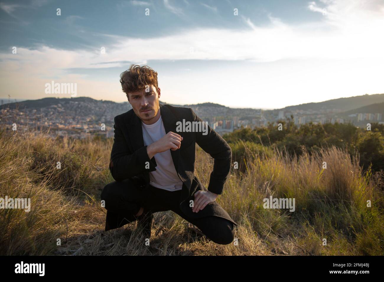 Adult bearded male in coat squatting on faded grass and looking at ...