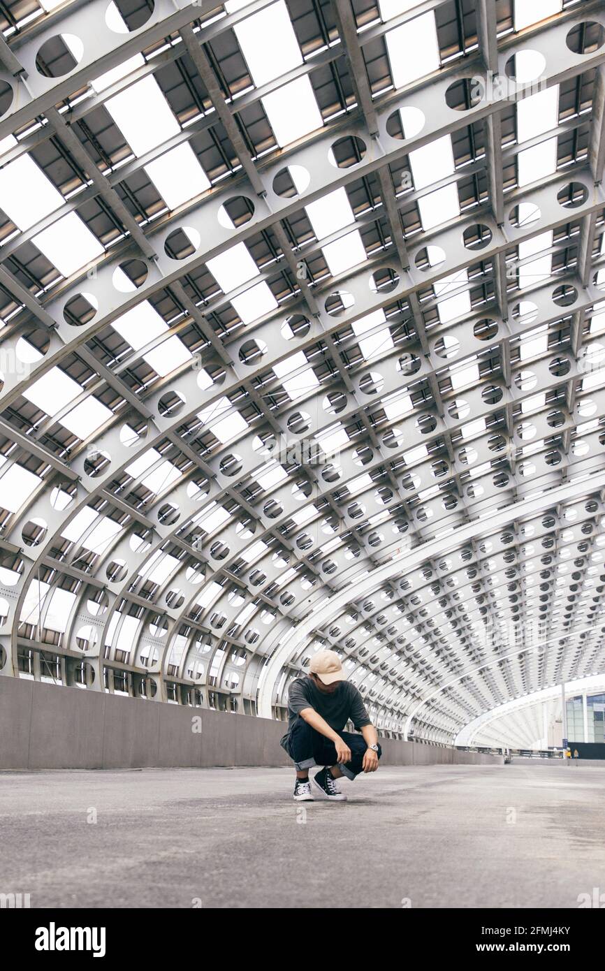 Full body faceless male sitting on haunches in creative pedestrian ...