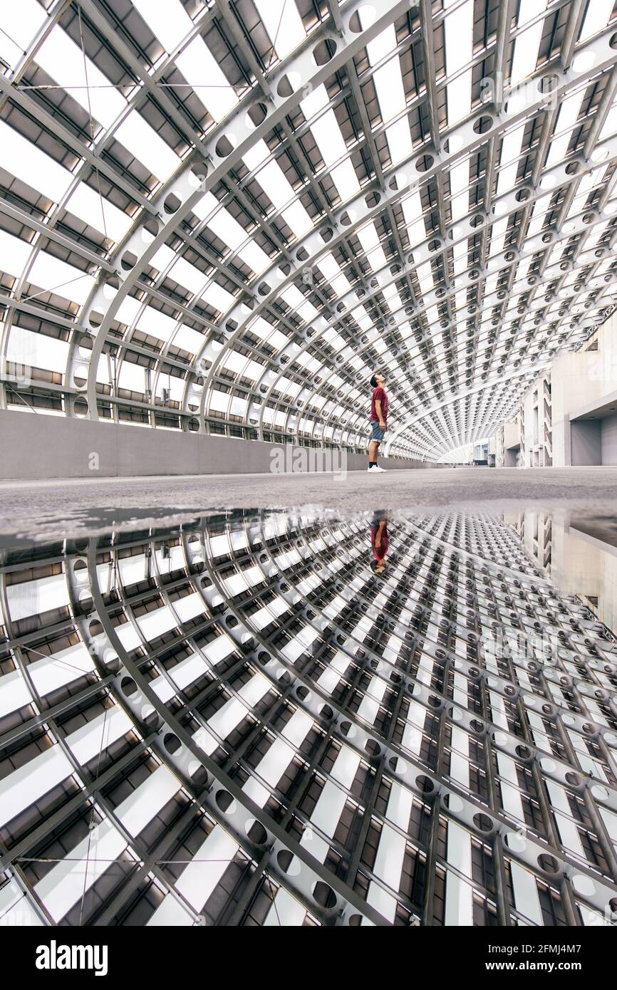 Unrecognizable male standing in unusual glass passage with geometric ...