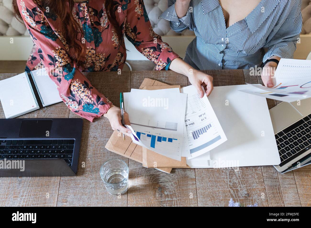 From above crop female coworkers gathering at desk with laptops and ...