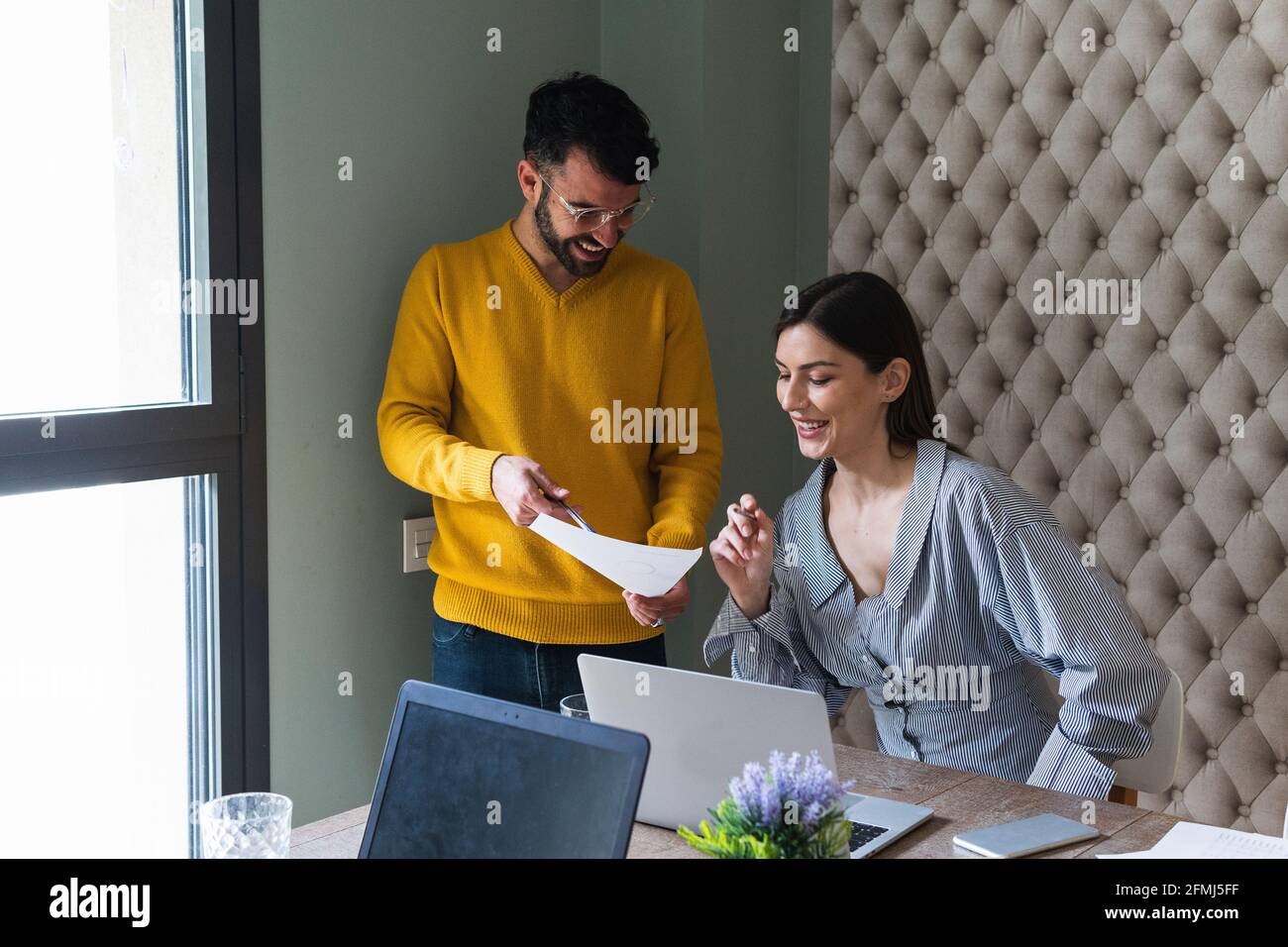 Happy young coworkers gathering and desk with laptops and discussing ...