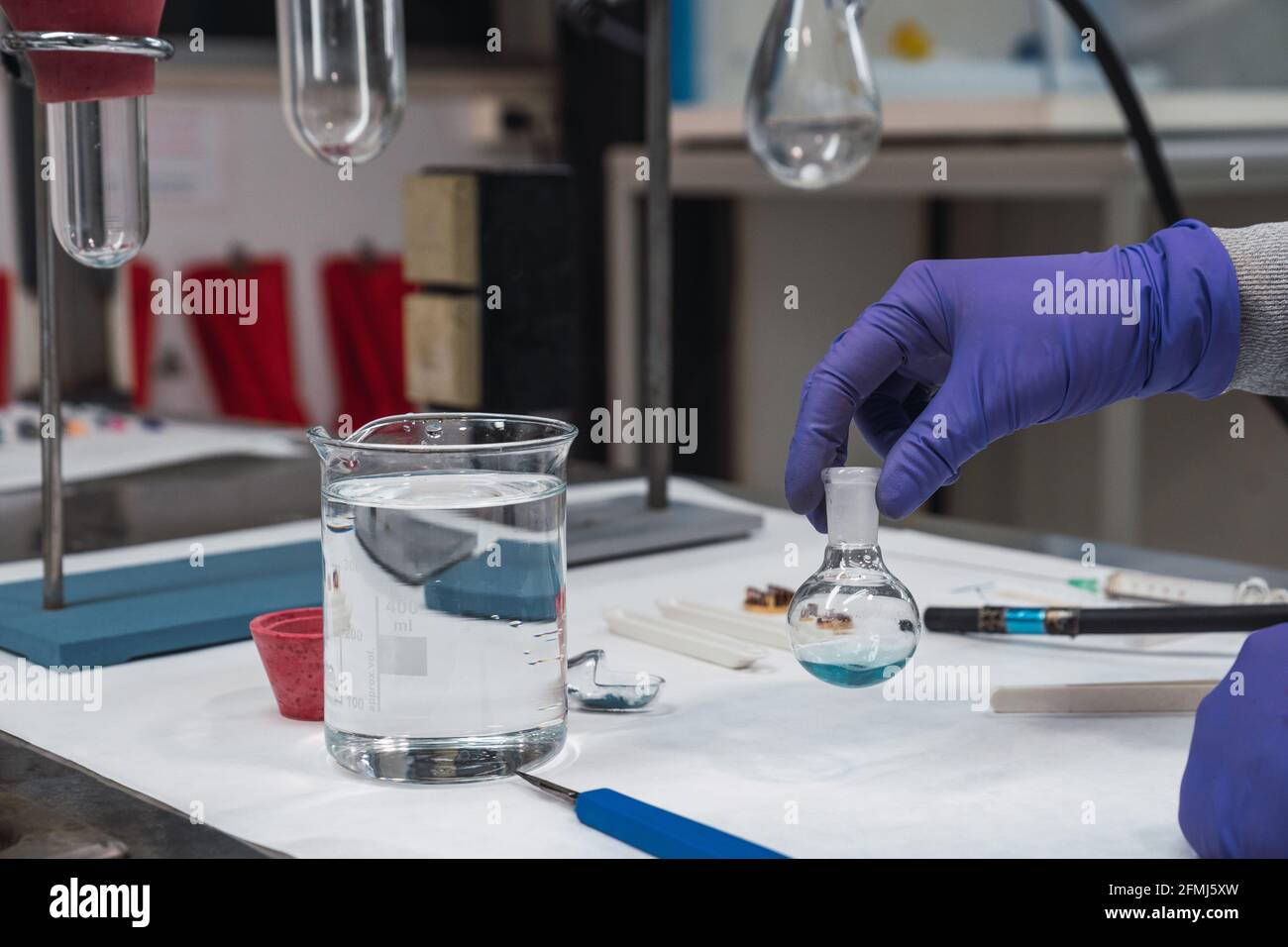 Crop anonymous scientist in protective gloves shaking blue chemical ...