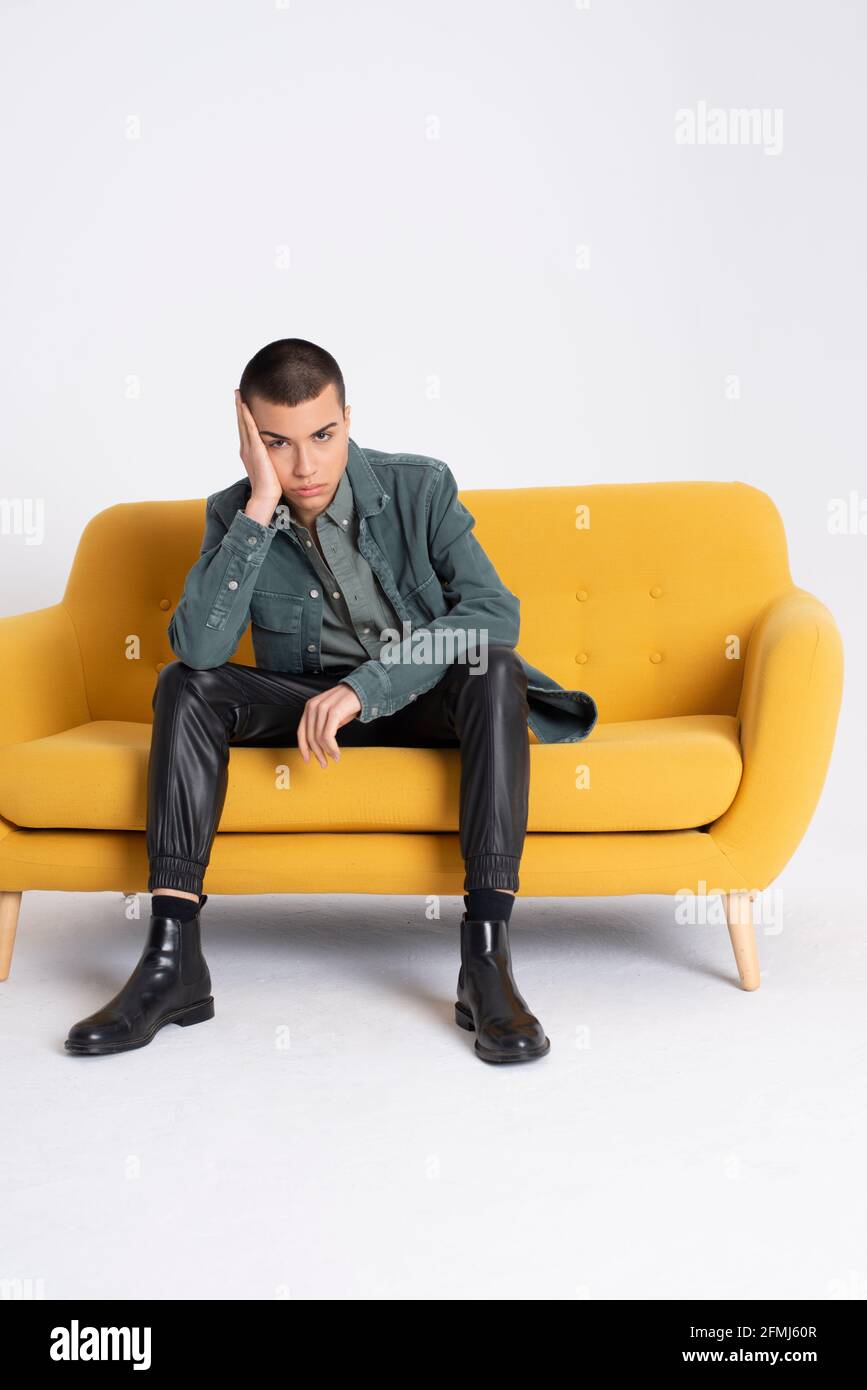 Young handsome male model in trendy clothes sitting on yellow couch on ...