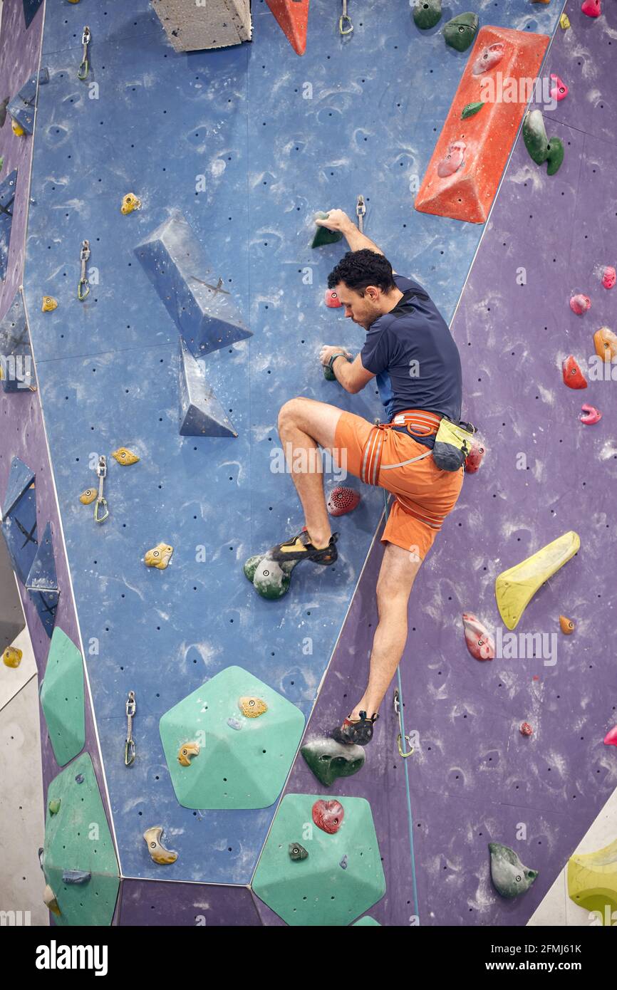 Back view of male mountaineer in harness climbing artificial wall in ...