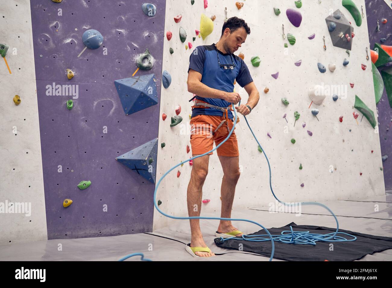From below of male alpinist preparing ropes and harness for climbing in ...