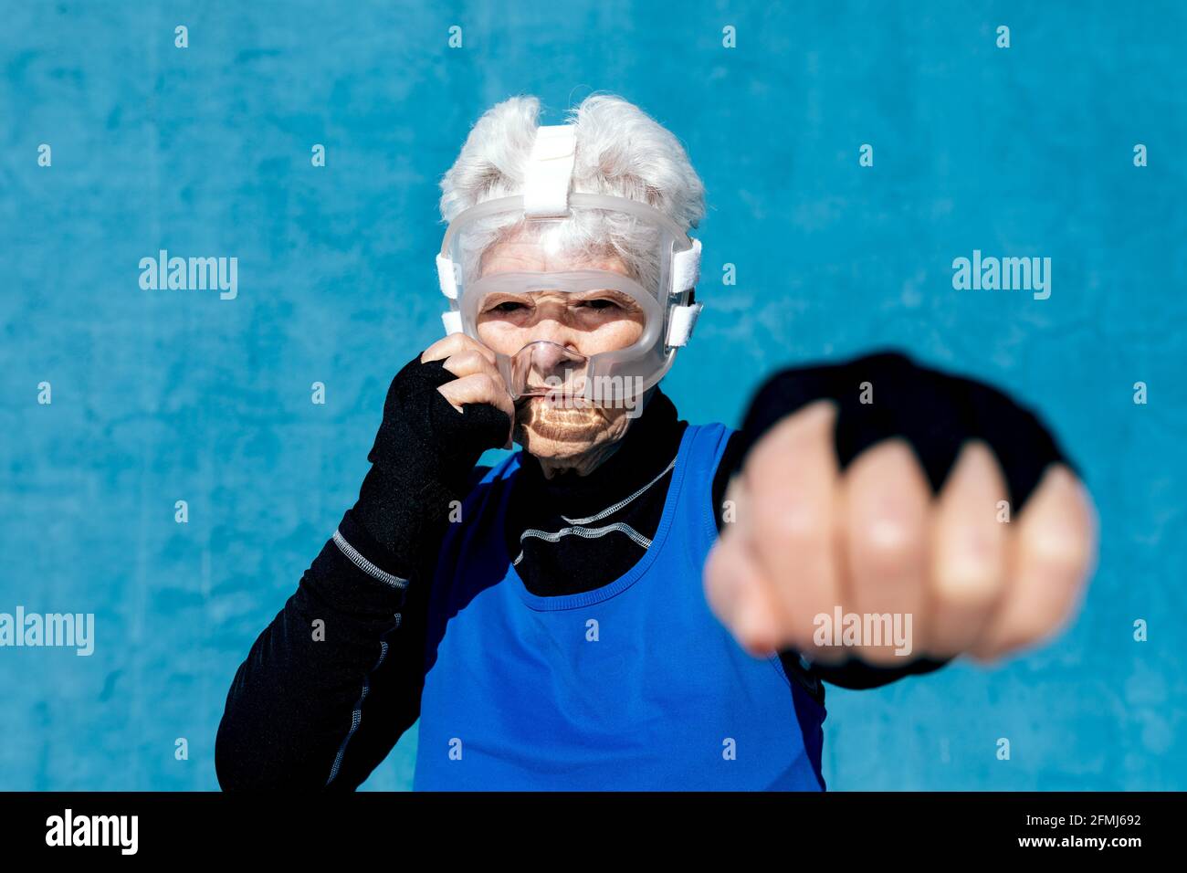 Focused mature female boxer in helmet and hand wraps punching air ...