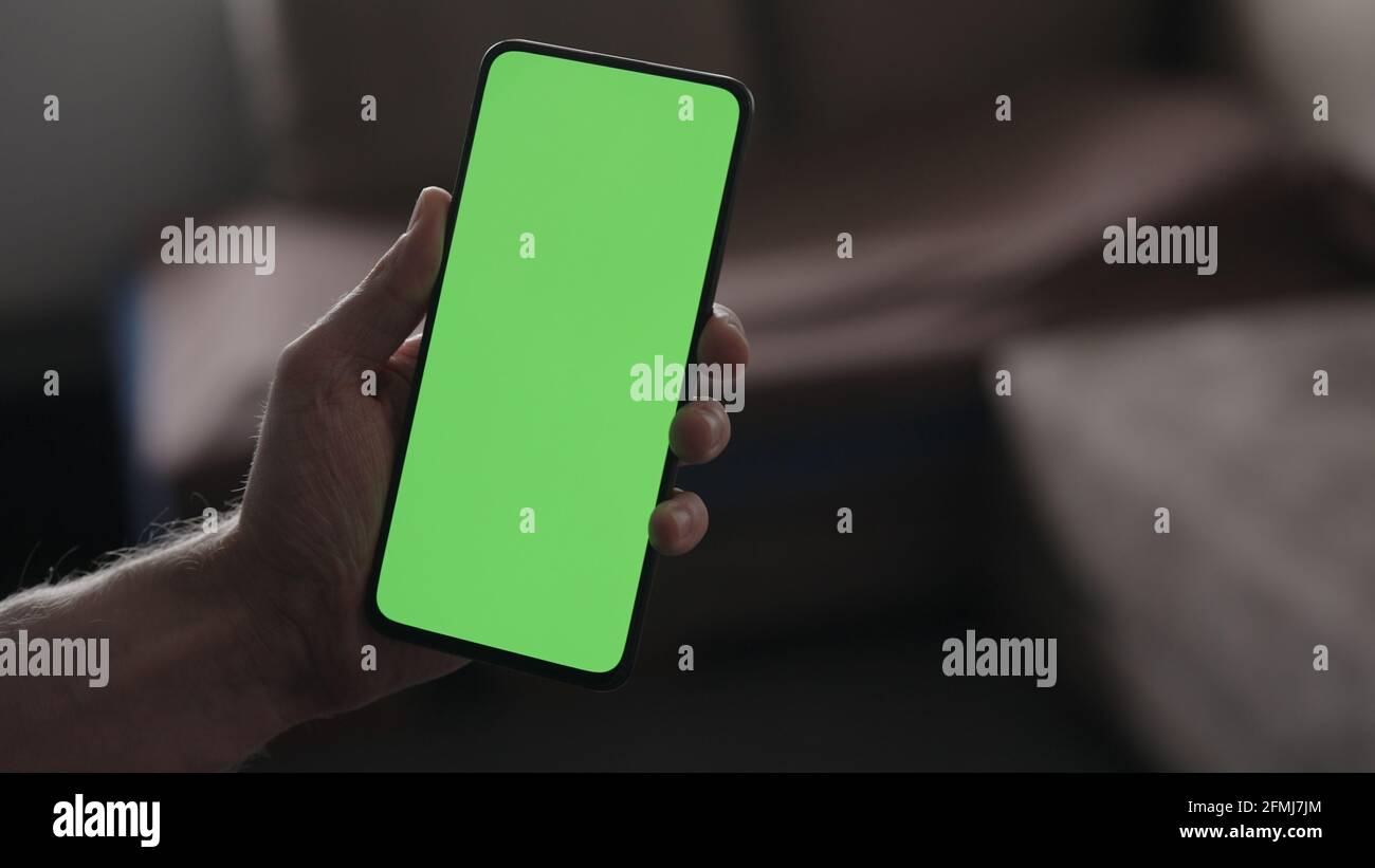 Man show smartphone with green screen while standing in living room ...
