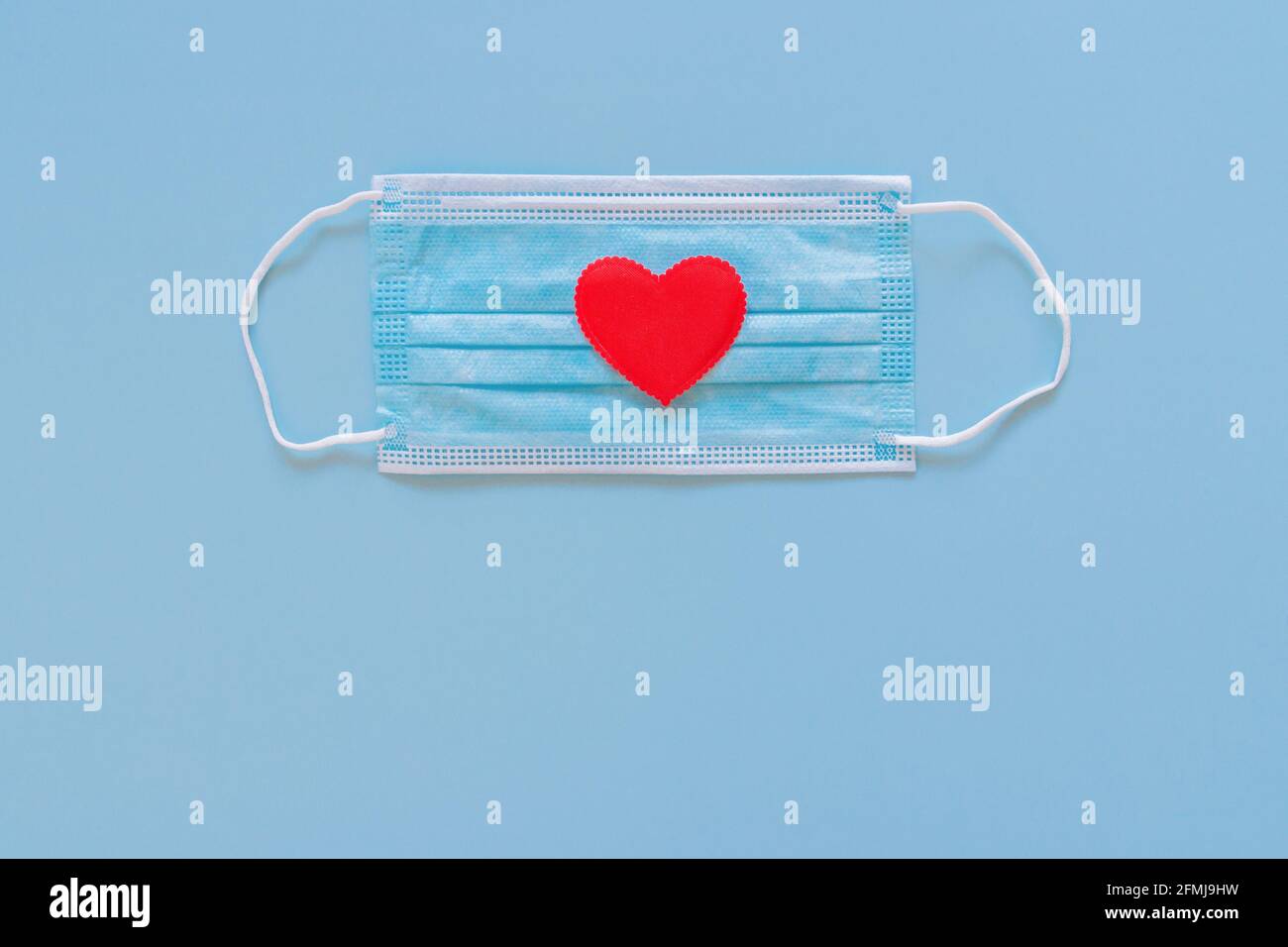 One red heart shape on medical protective mask on blue background ...
