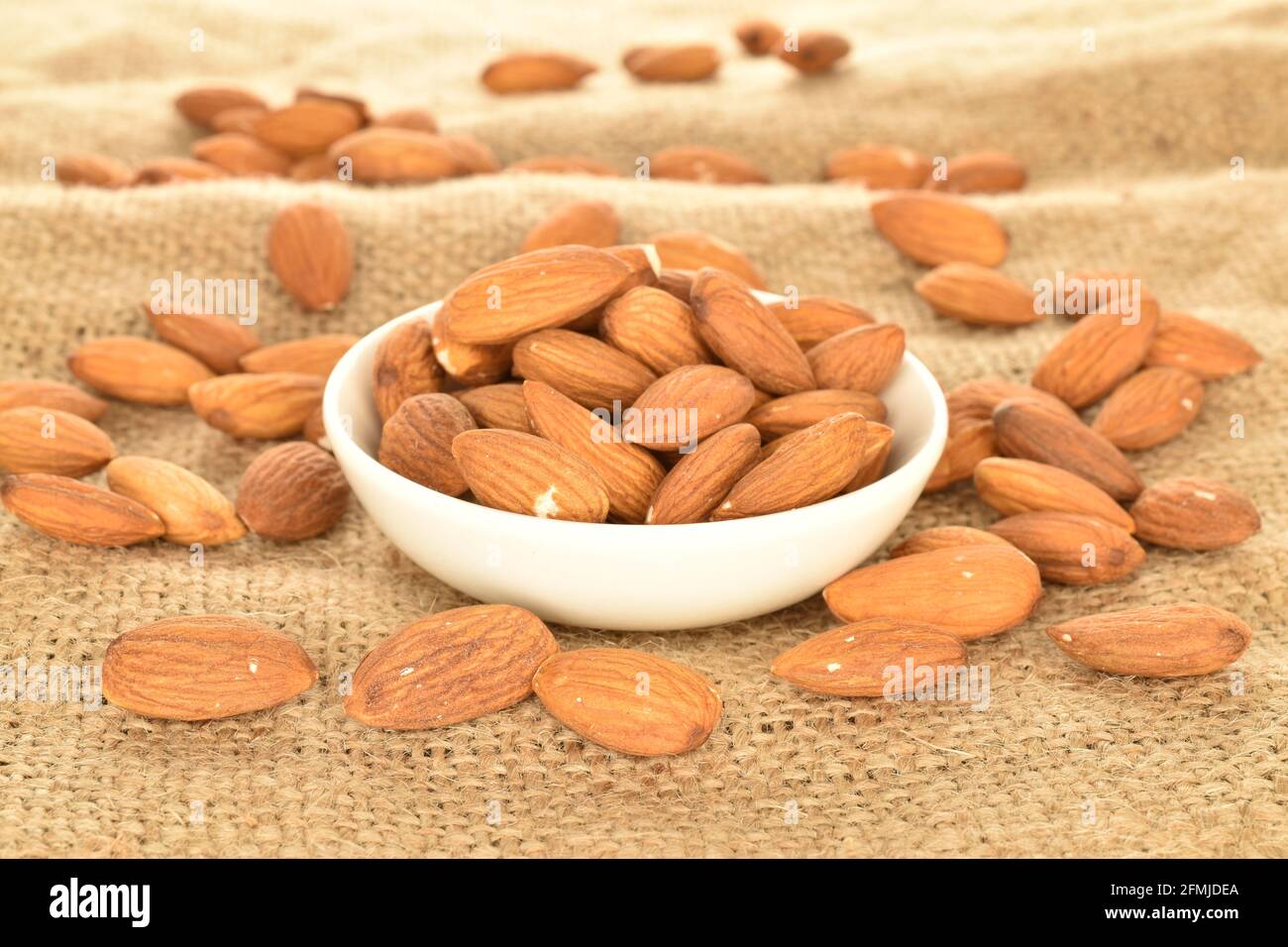 Several grains of peeled raw, organic almonds in a white plate, close ...