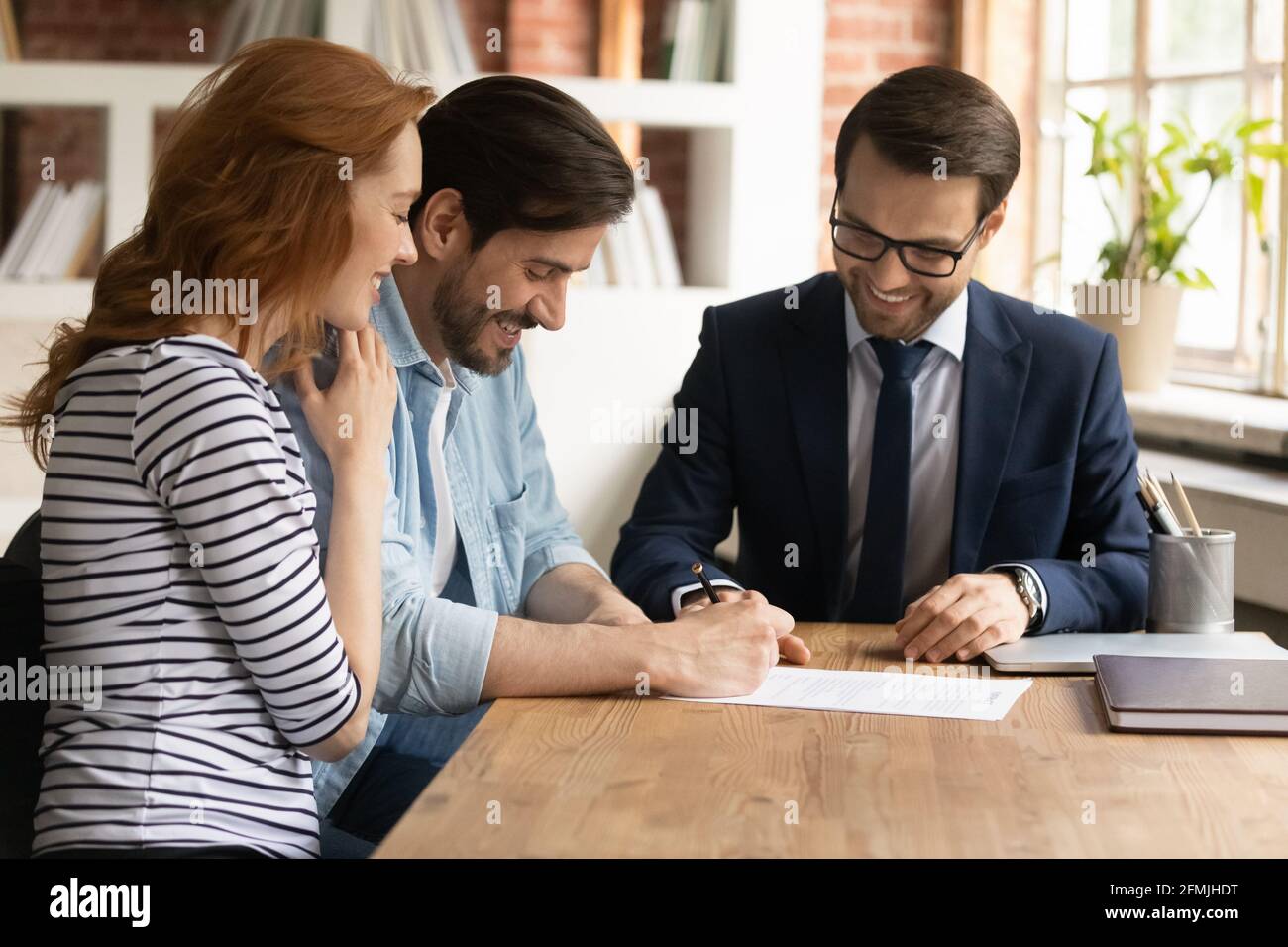 Happy millennial couple signing contract with manager at meeting Stock ...
