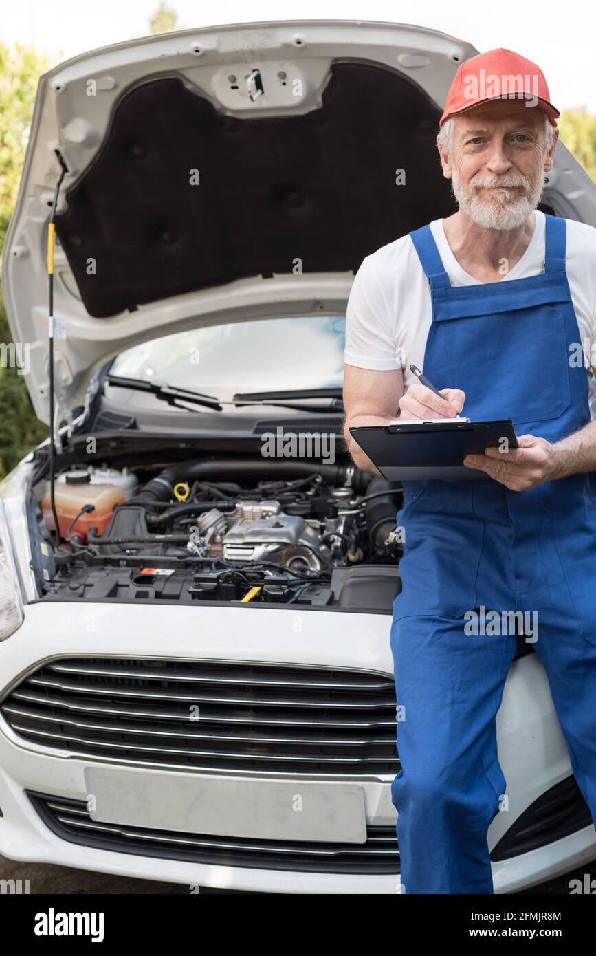 Car mechanic checking a car engine and writing on clipboard Stock Photo ...