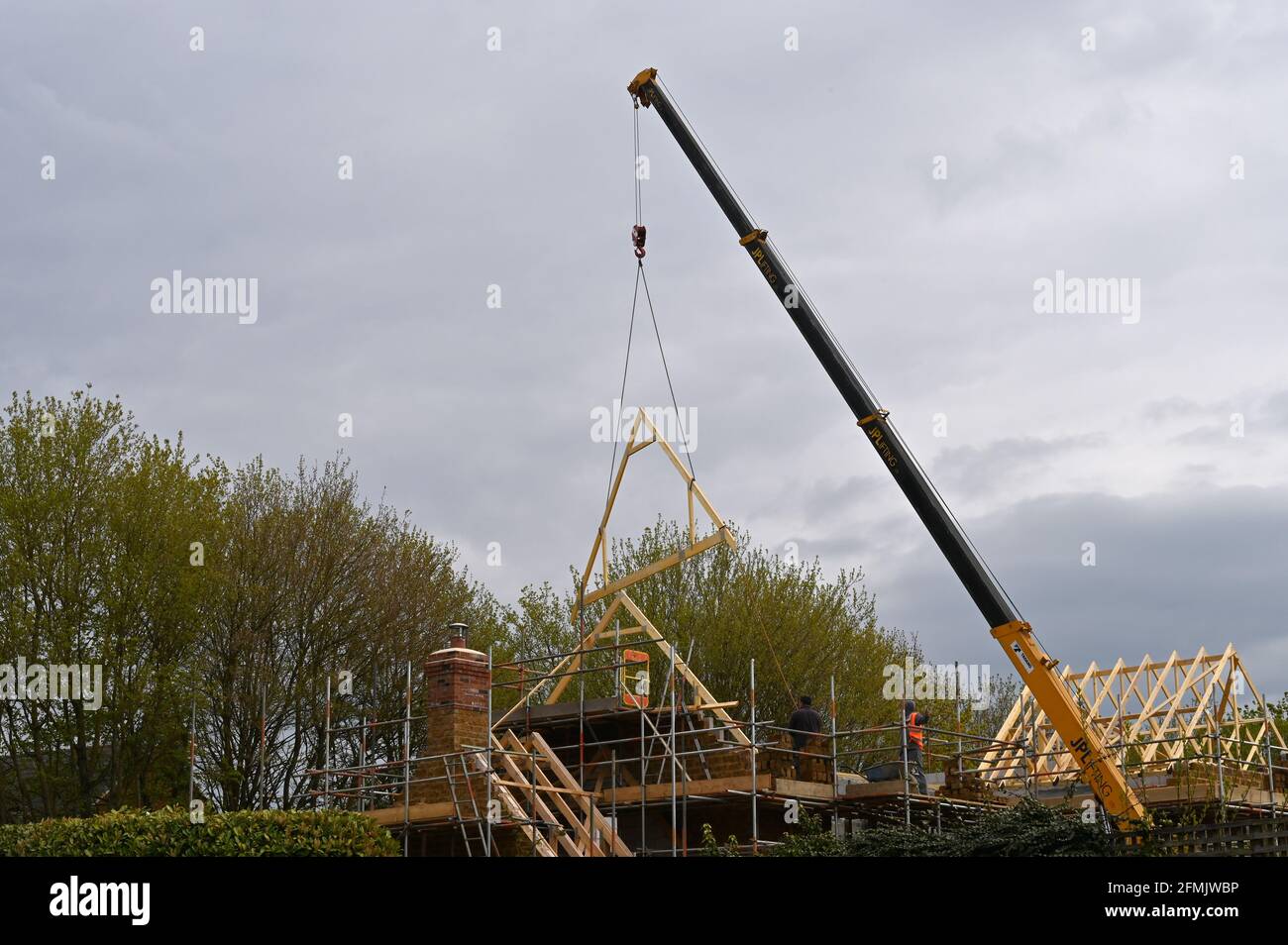 Crane in the course of lifting roof trusses into position on a building ...