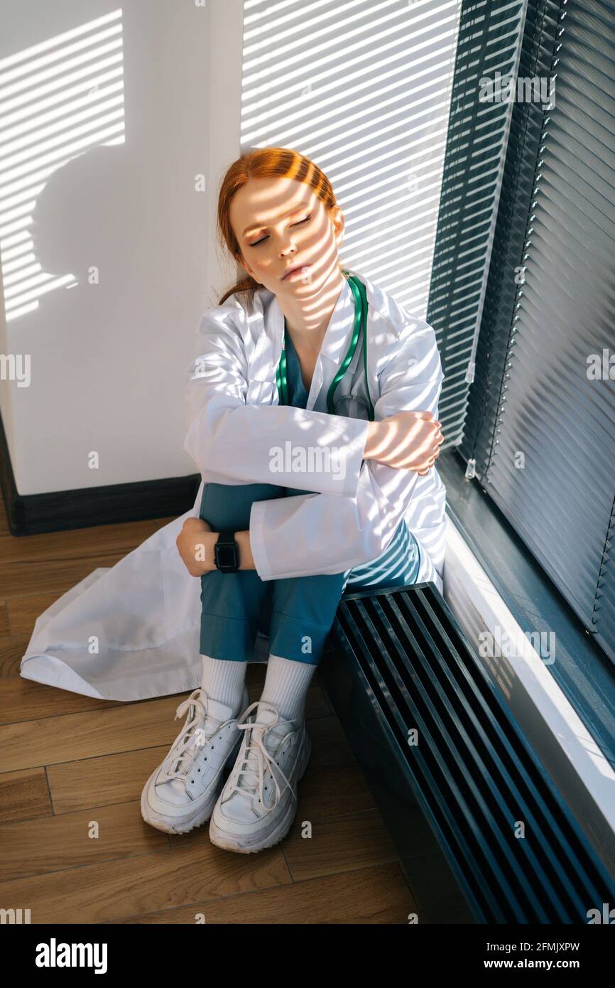 Close-up of frustrated sad young female doctor in white coat sitting on ...