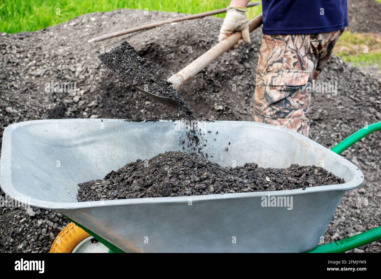 unidentified man pours gravel into a wheelbarrow. as part of a ...