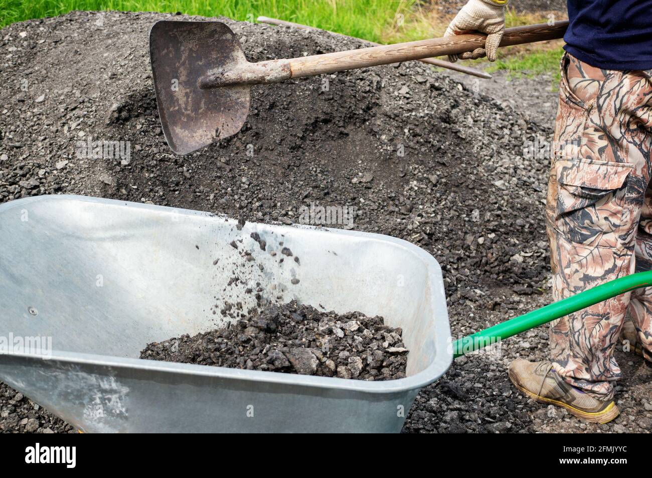unidentified man pours gravel into a wheelbarrow. as part of a ...