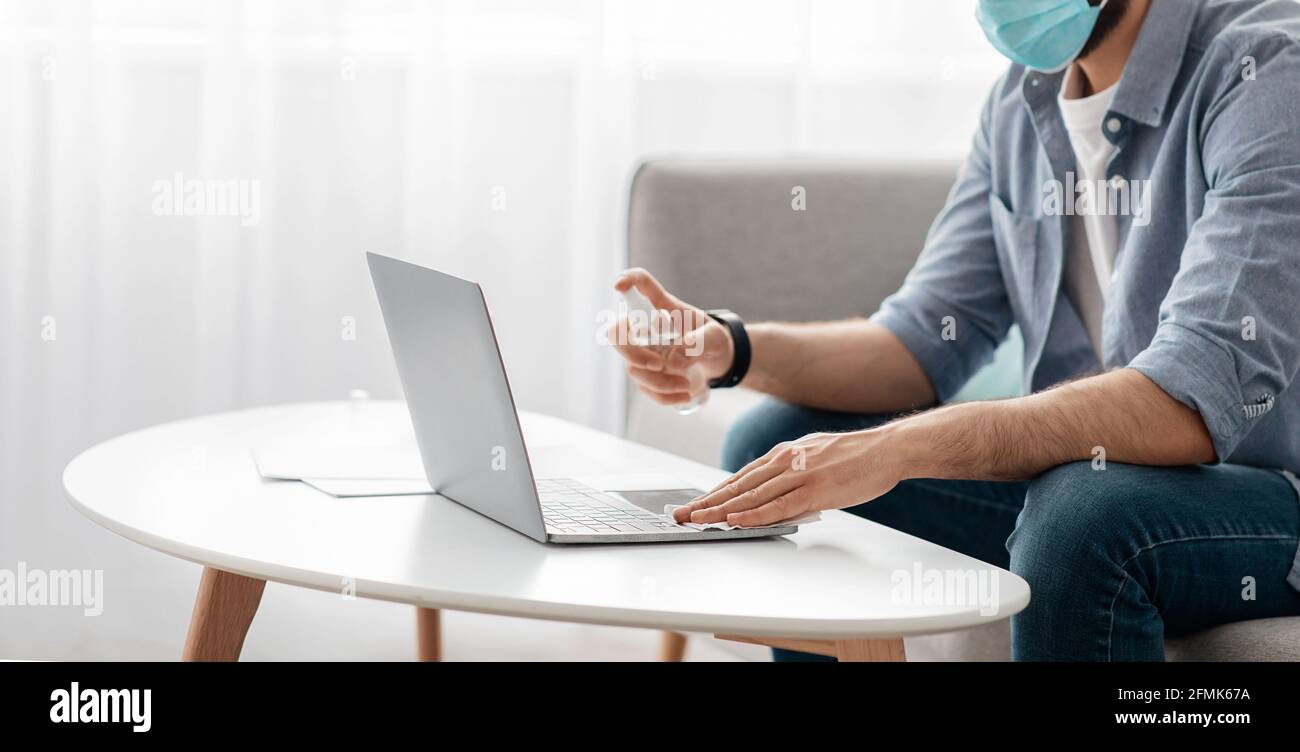 Unrecognizable man sanitizing laptop keyboard surface with disinfectant ...