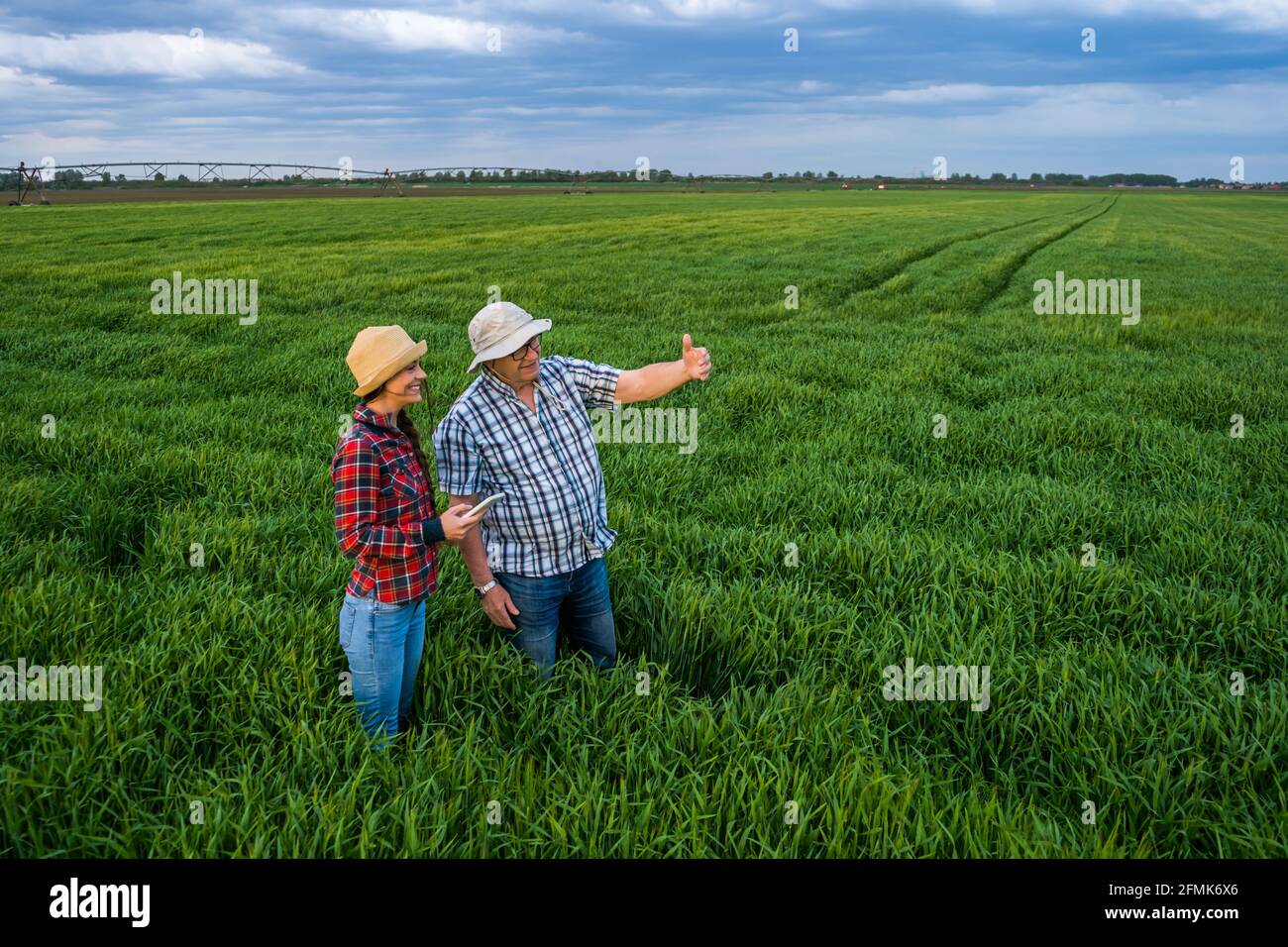 Two generations farmers are standing in their barley field and ...