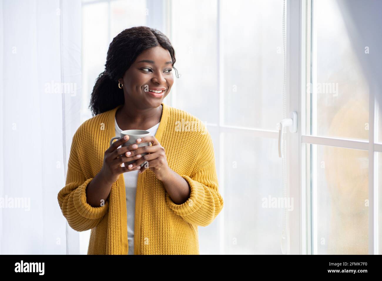 Pretty black lady in casual standing next to window in living room ...