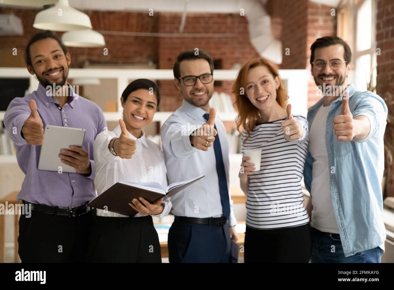 Smiling diverse employees group showing thumbs up, looking at camera ...