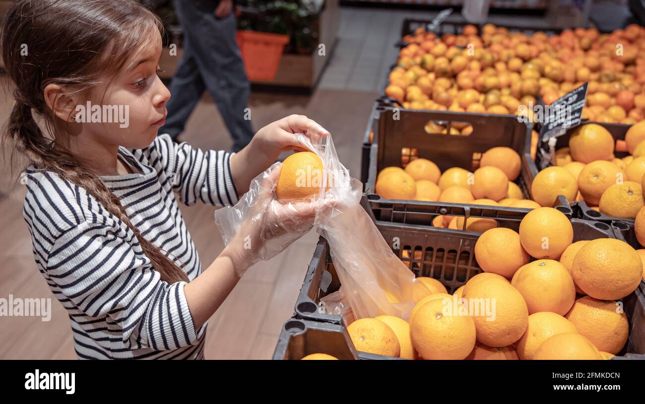 A funny little girl in a grocery store chooses oranges to buy Stock ...