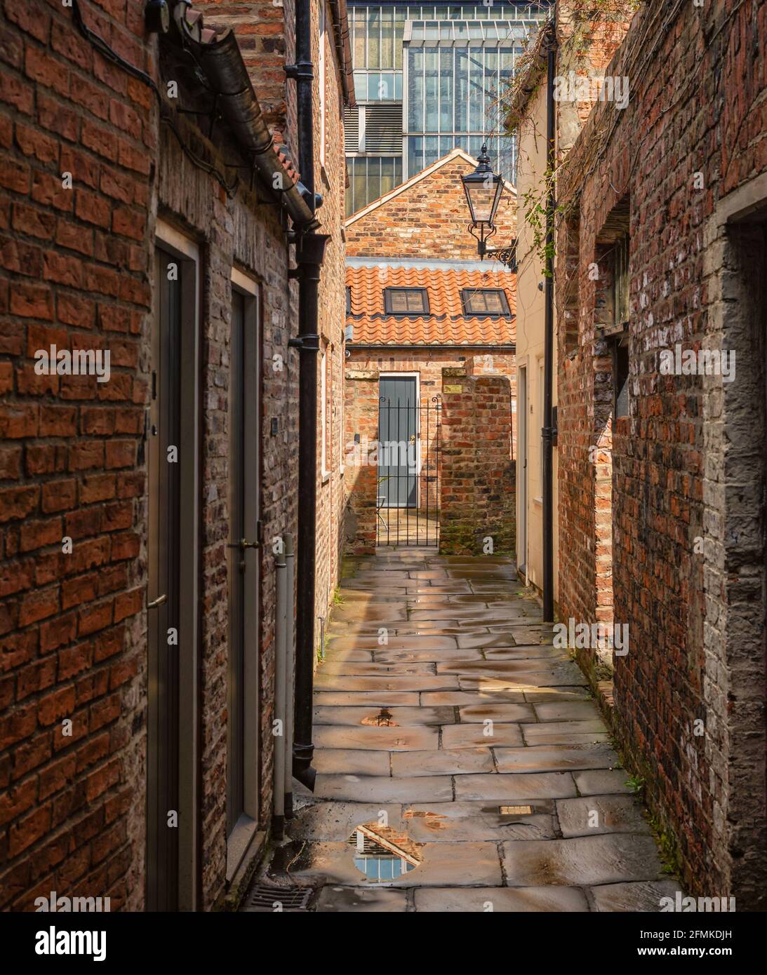 An narrow alleyway leading to a gated property and a glass building ...