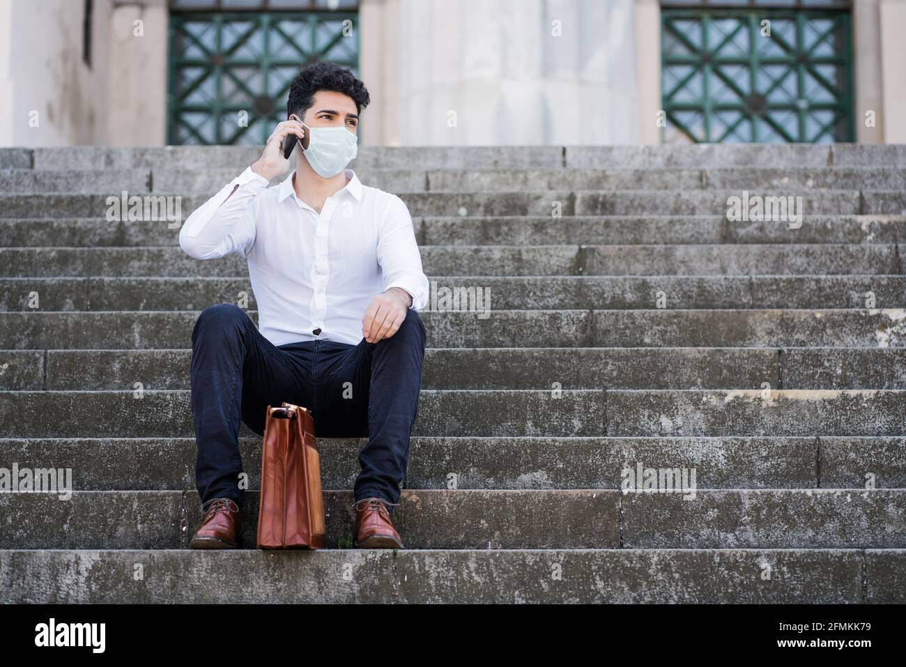 Portrait of business man wearing face mask and using his mobile phone ...