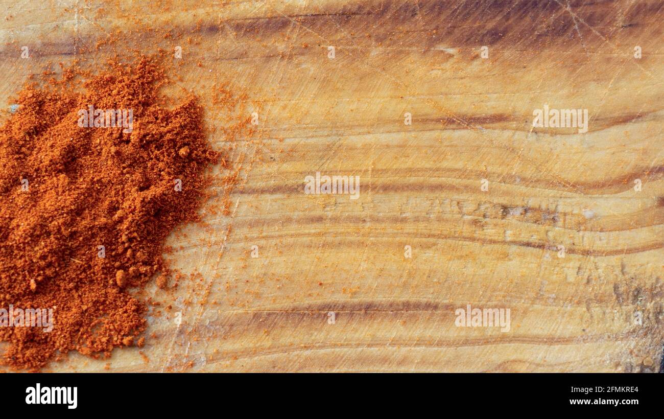 Red paprika powder over a rustic wooden cutting board background with ...