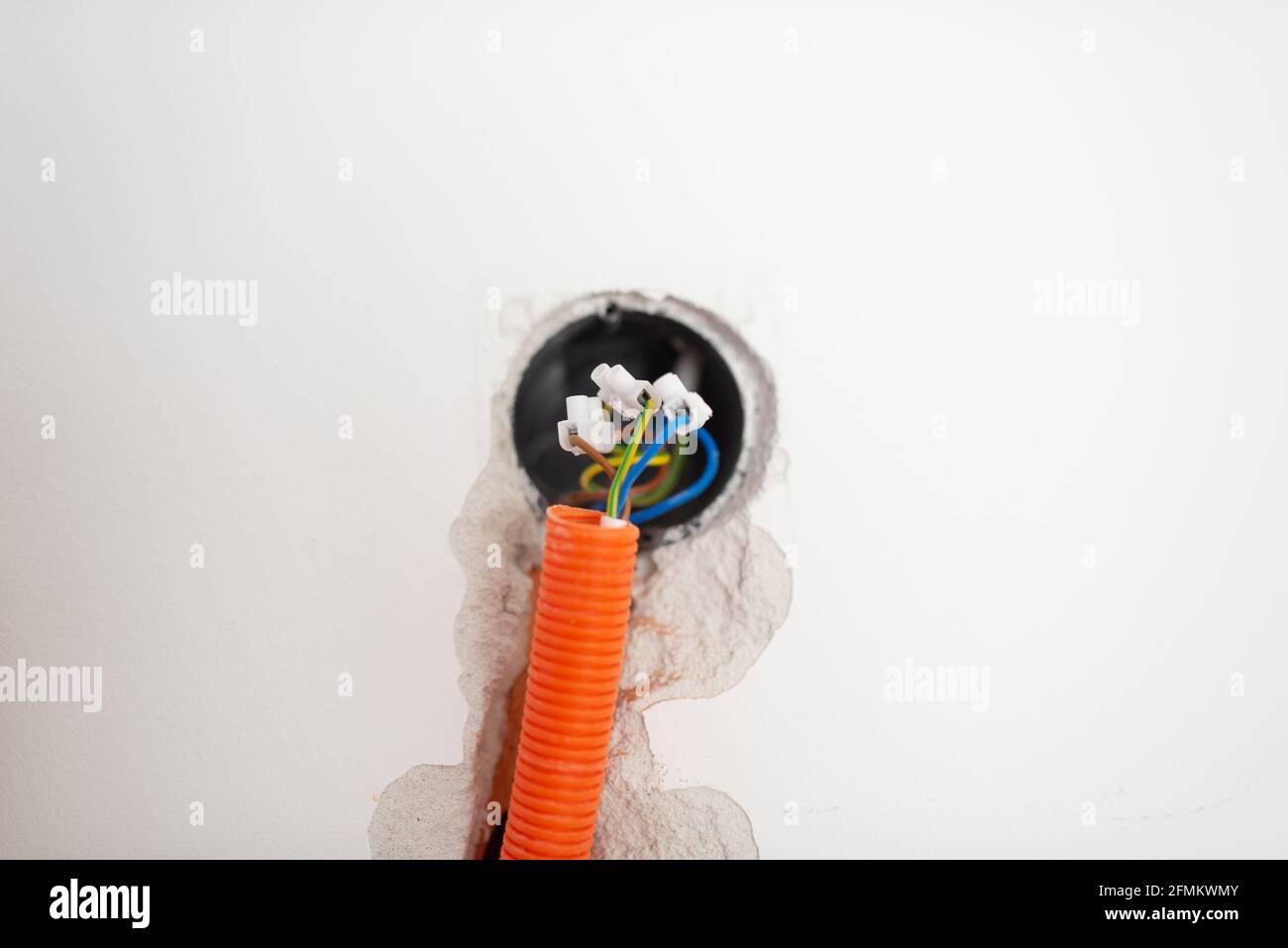 Round hole in the wall with electrical wires and orange corrugated tube ...