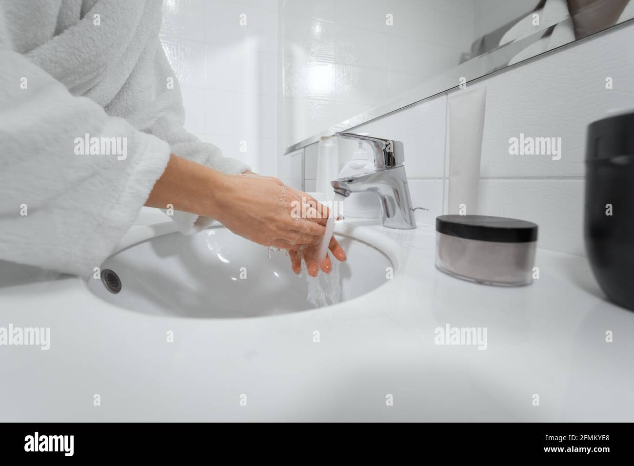 Side view of woman in white robe washing hands with soap in bathroom at ...