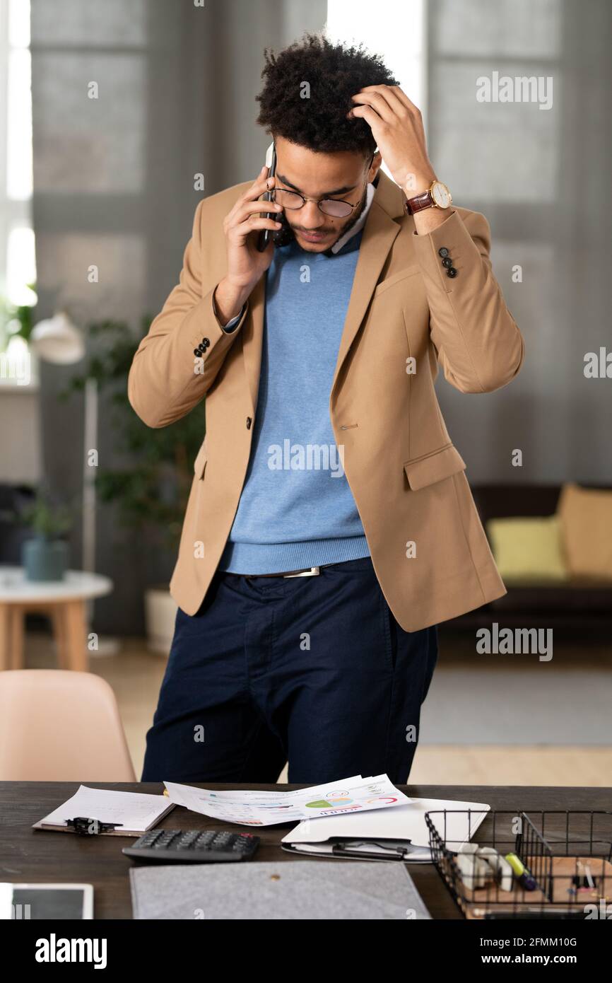 Puzzled young mixed race manager with afro hairstyle standing at table ...