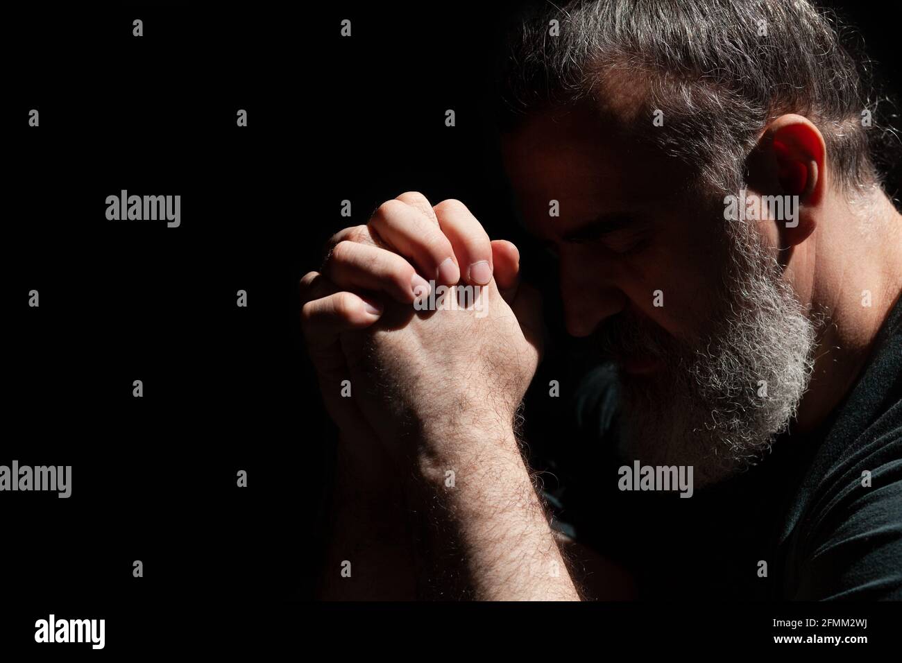 Bearded man holding hands in prayer in the sun, face hidden in shadow ...