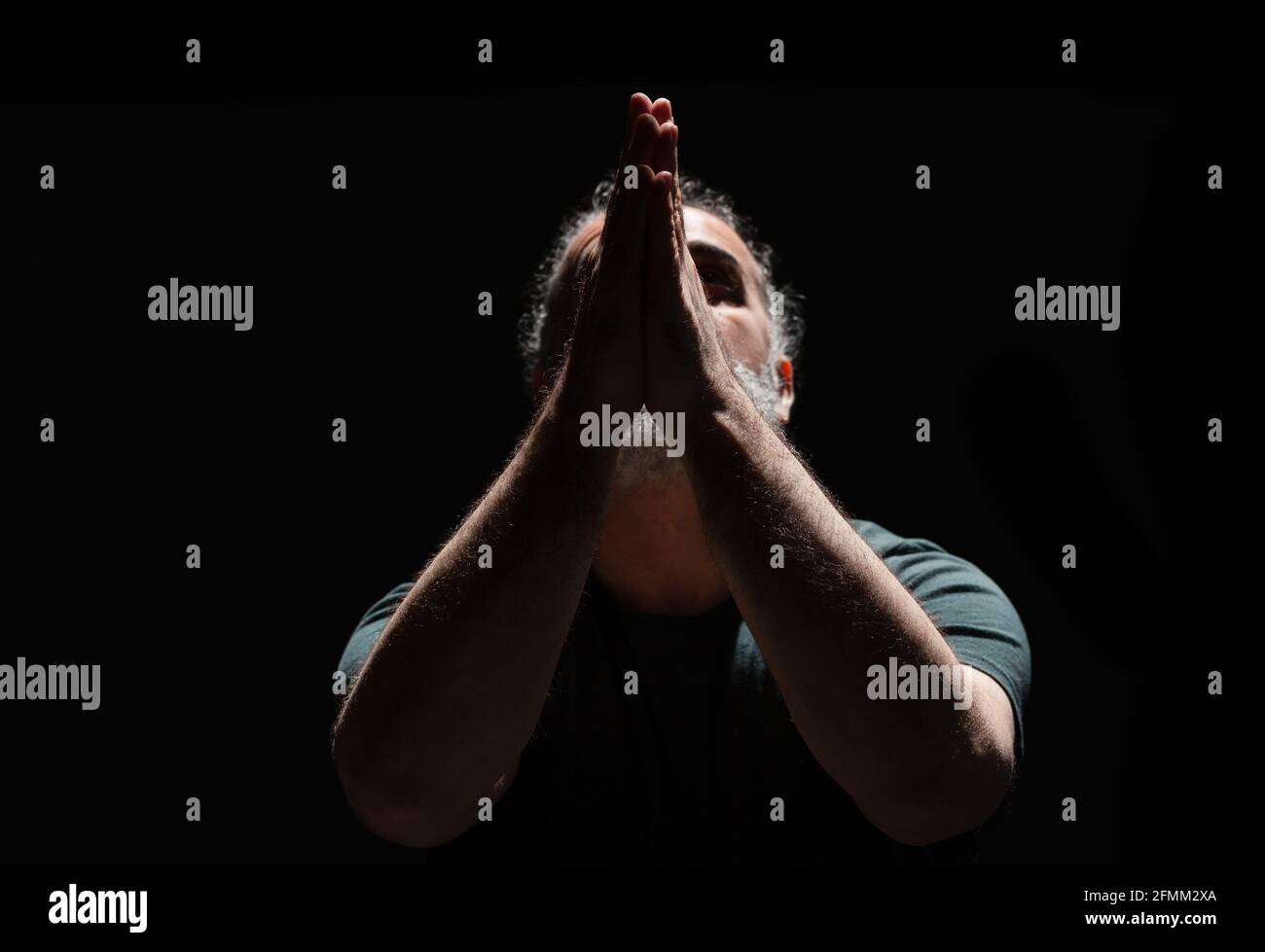 Man holding hands in prayer, face looking up to the sky, surrounded ...