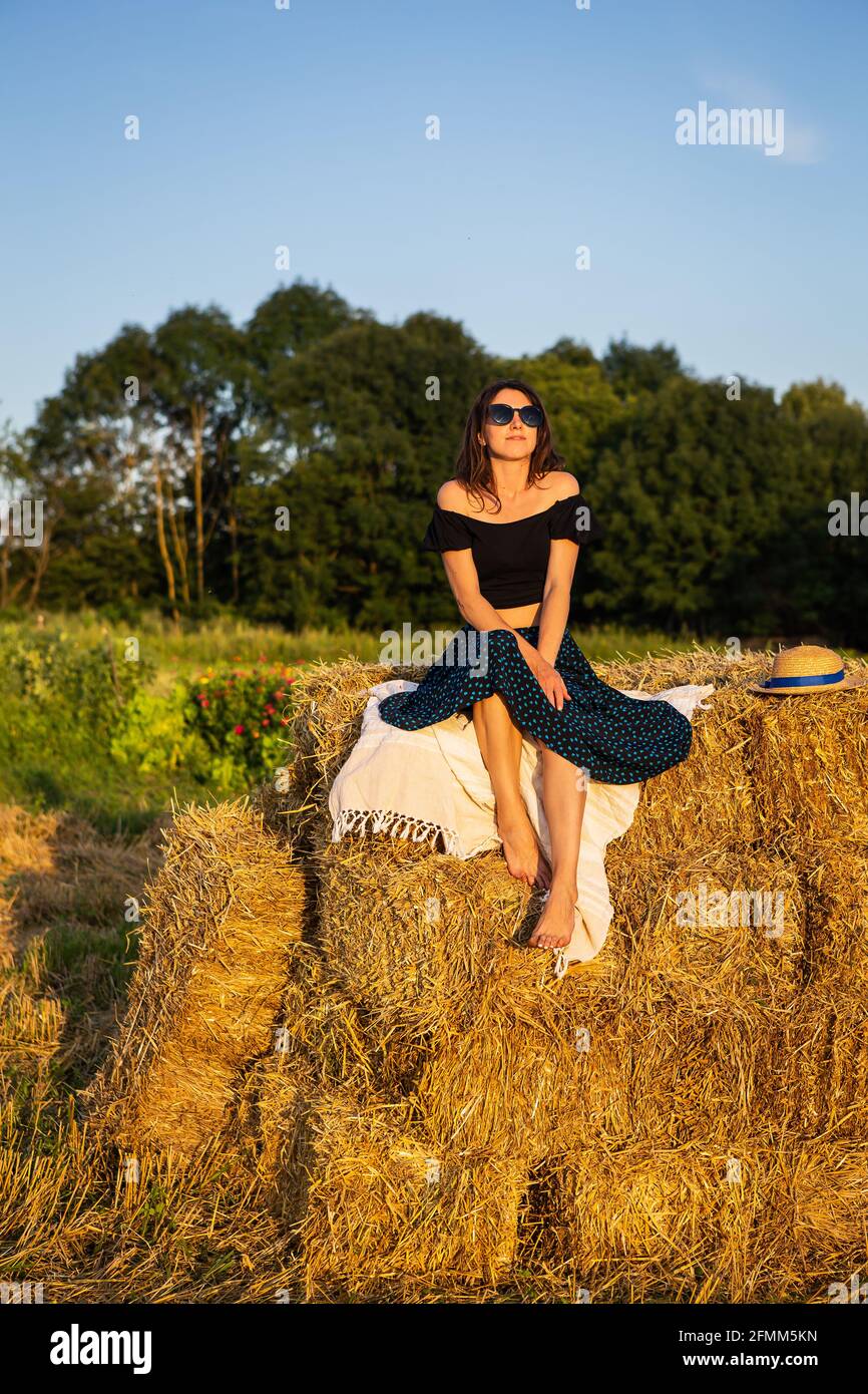 Young beautiful woman in black glasses looks at the setting sun, sits ...