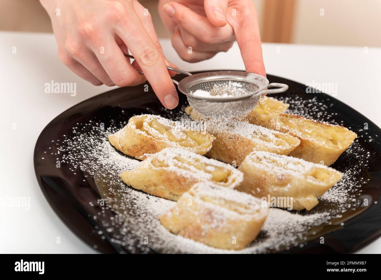 Women hands sprinkles icing sugar on the apple roll. Strudel feed Stock ...